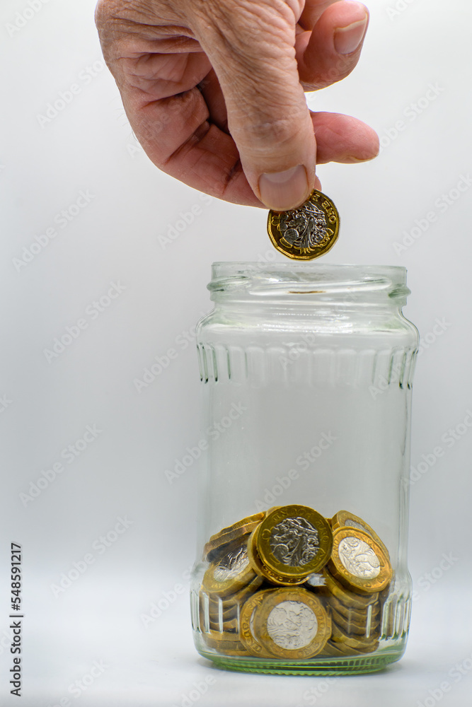 British Currency pound coins, putting money into a jar, saving and ...