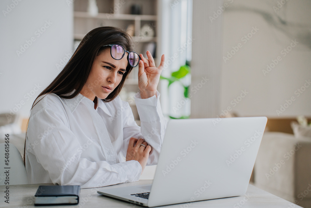 Foto de Perplexed young Brunette Caucasian businesswoman in white shirt sits at desk with laptop ...
