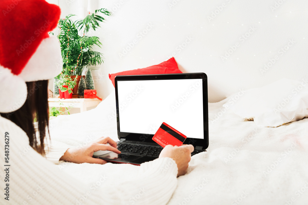 Faceless woman in santa hat lying on bed at home with laptop and ...
