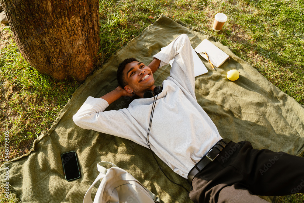 Young black man smiling while lying on blanket under tree in park Stock ...