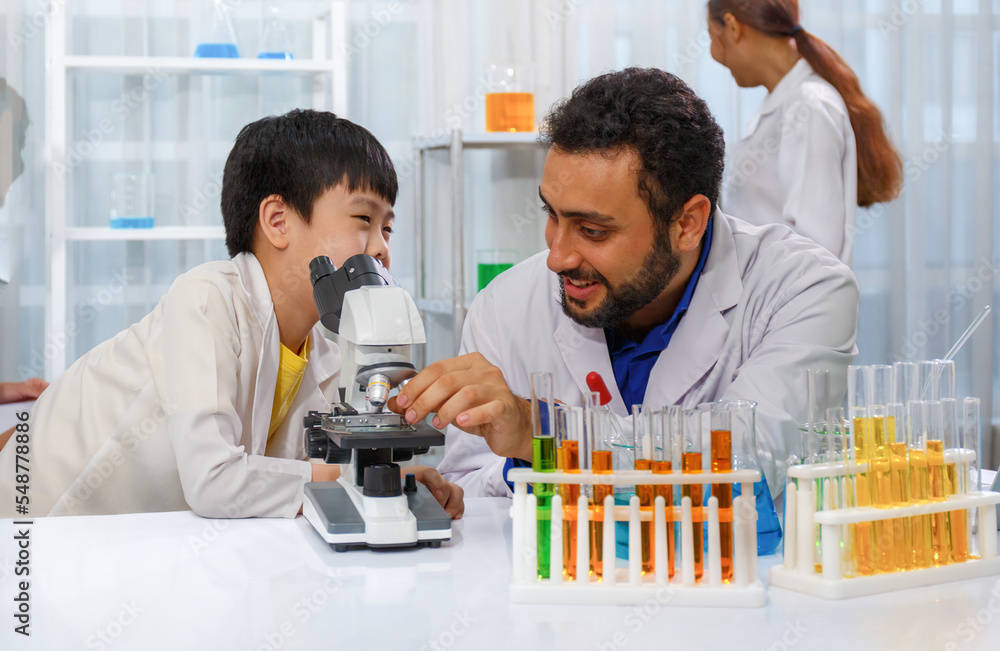 male teacher sitting at classroom desk with male student using ...