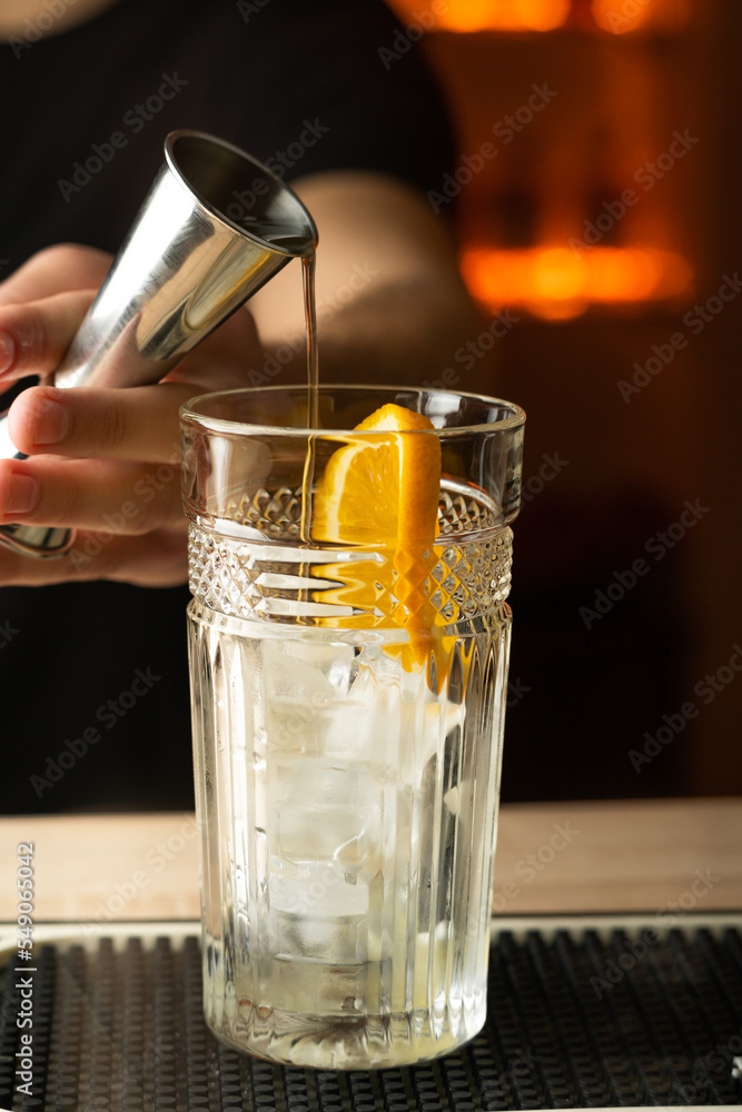 Bartender pouring a gin from the steel jigger to the glass on the bar ...
