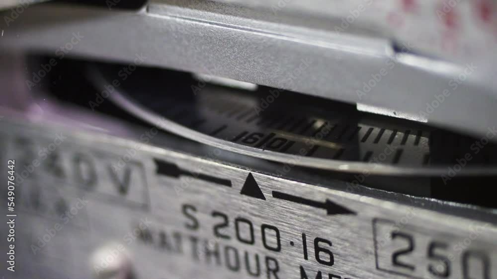 A close-up of an electric meter measuring dial. A turning rotor disc ...