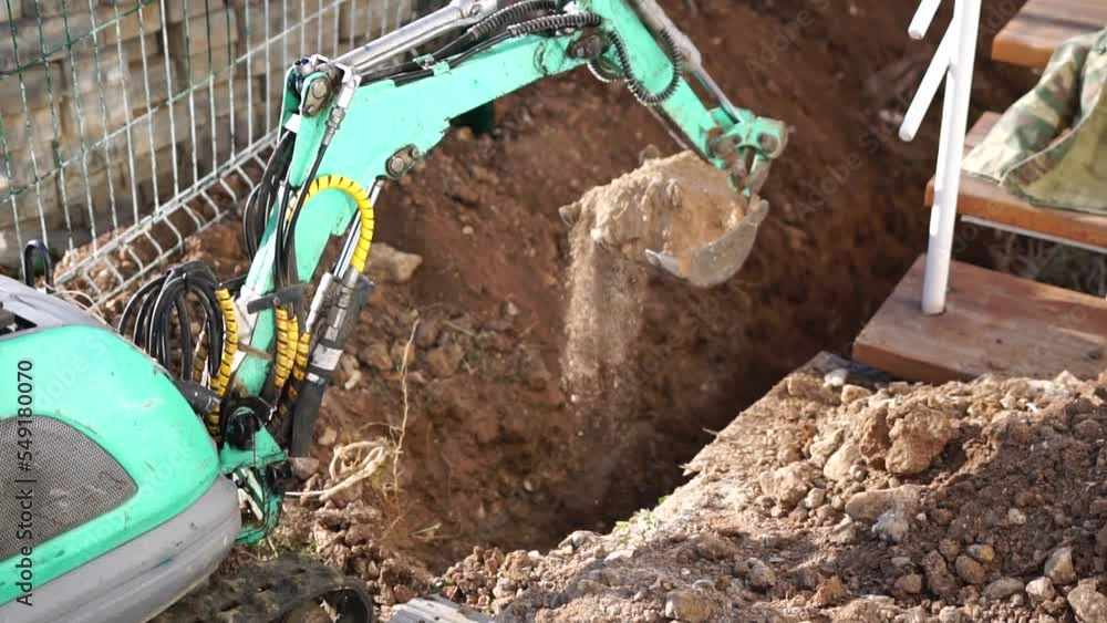 Mini excavator digs a trench to lay pipes. Close up of an excavator digging a deep trench. An ...