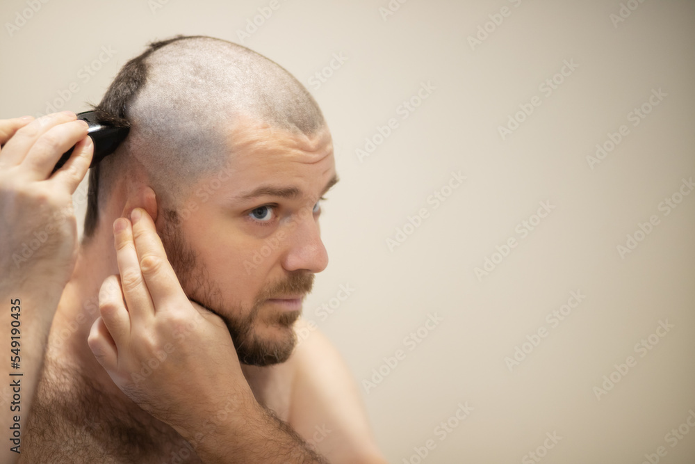 self haircut, a man cuts his head with a clipper at home in front of a ...