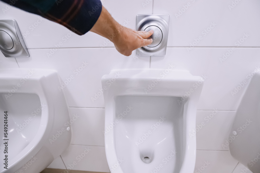 Male hand flashing water in urinals in a public men's toilet. The ...