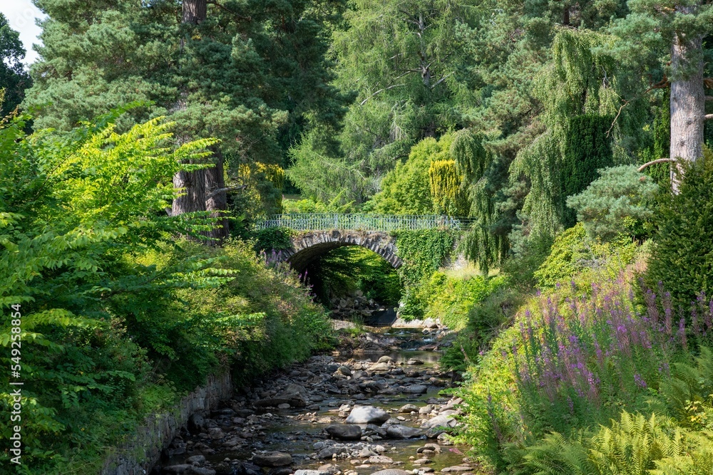Arch of a rural bridge over a dried river with lush greenery on its ...