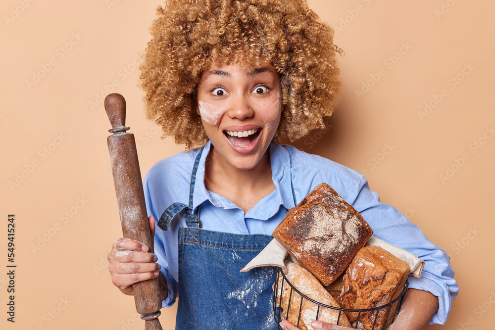 Curly haired woman holds rolling pin and variety of crusty bread ...