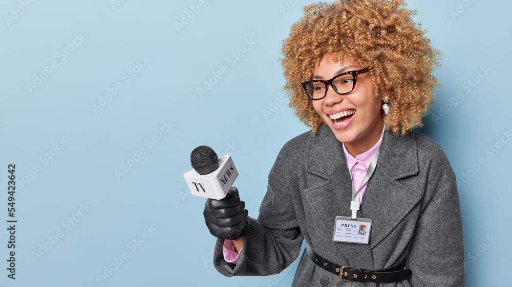 Horizontal shot of overjoyed female correspondent holds microphone and ...