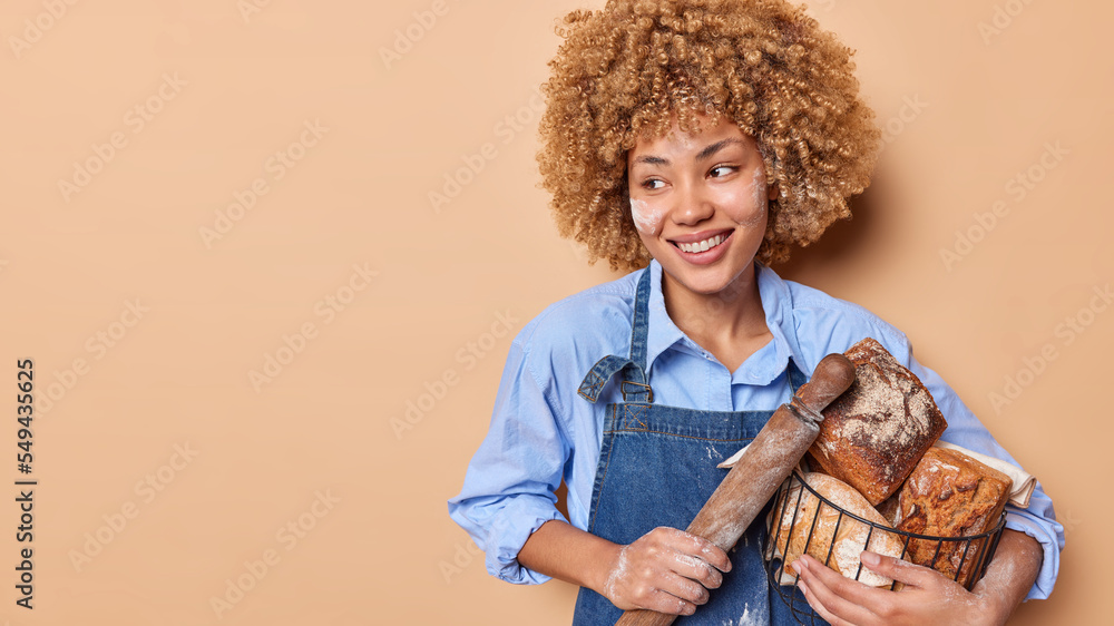 Cheerful cury haired female baker poses with crusty freshly baked bread ...