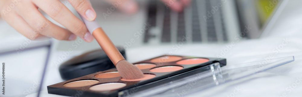 Hands of woman with learning makeup with brush on cheek on laptop ...