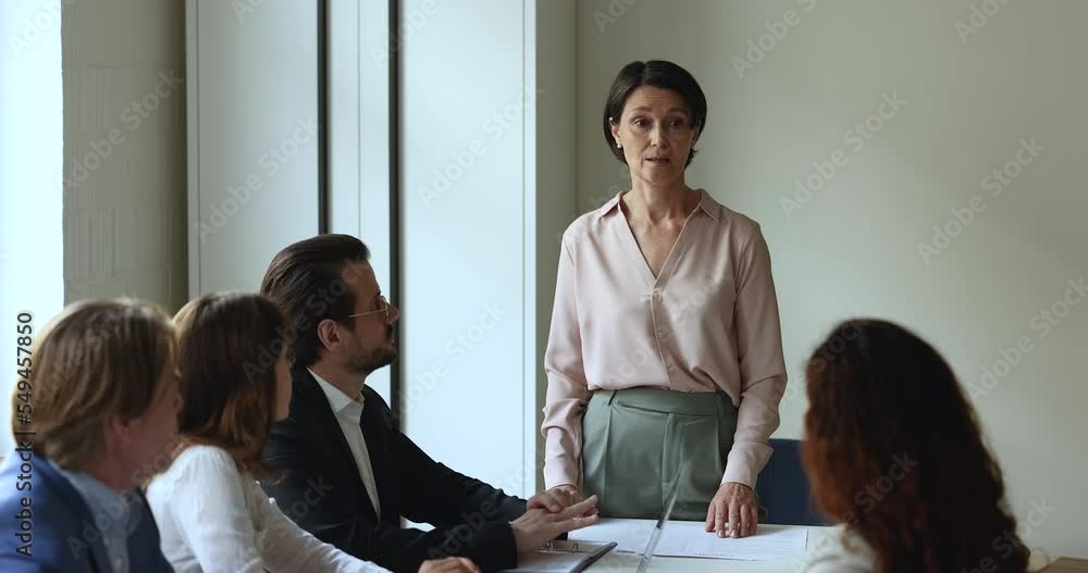 Group briefing lead by mature business woman makes speech standing in ...