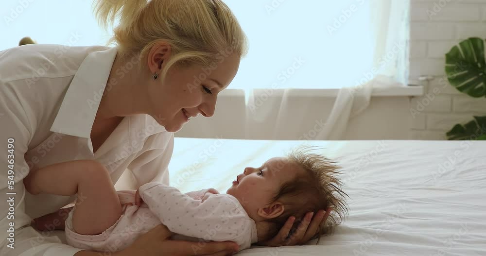 Happy loving blonde mom cuddling child lying on back in bed, bending ...