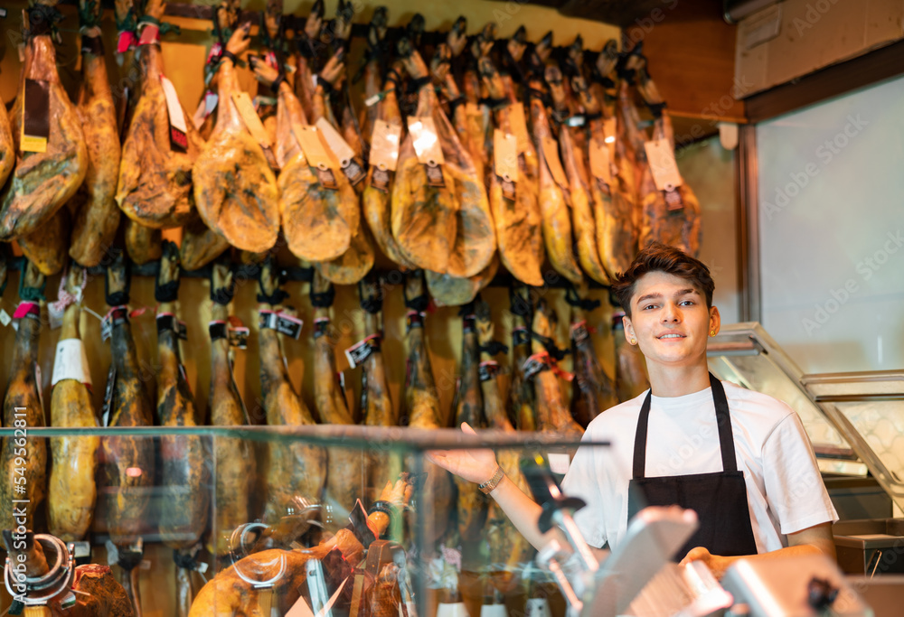 Smiling young salesman in black apron standing near rack with delicious ...
