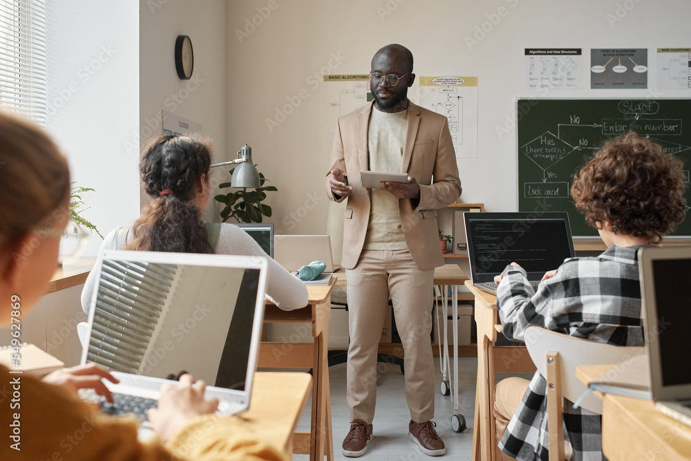 African American teacher explaining to group of children how to work on ...