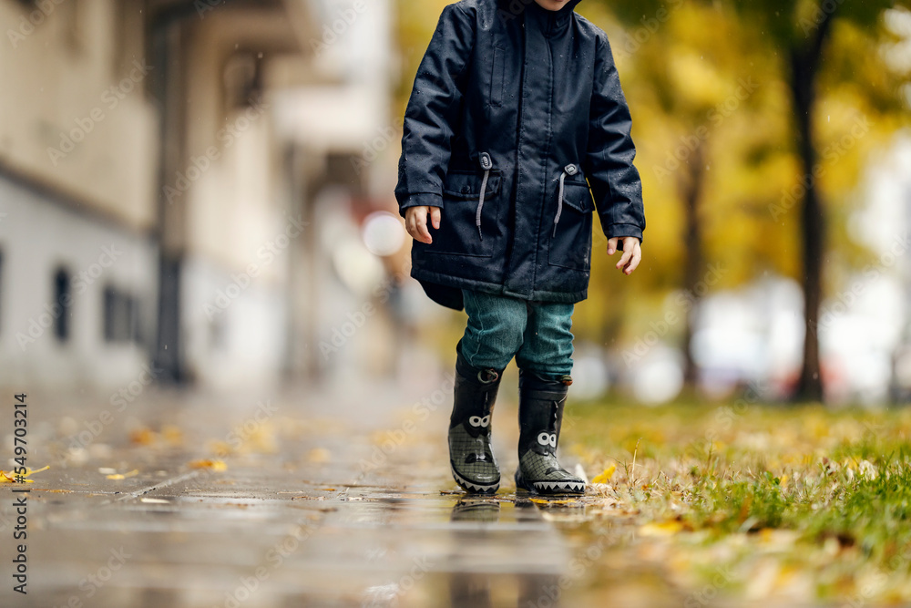 Cropped picture of a playful little boy playing with rain puddle on the ...