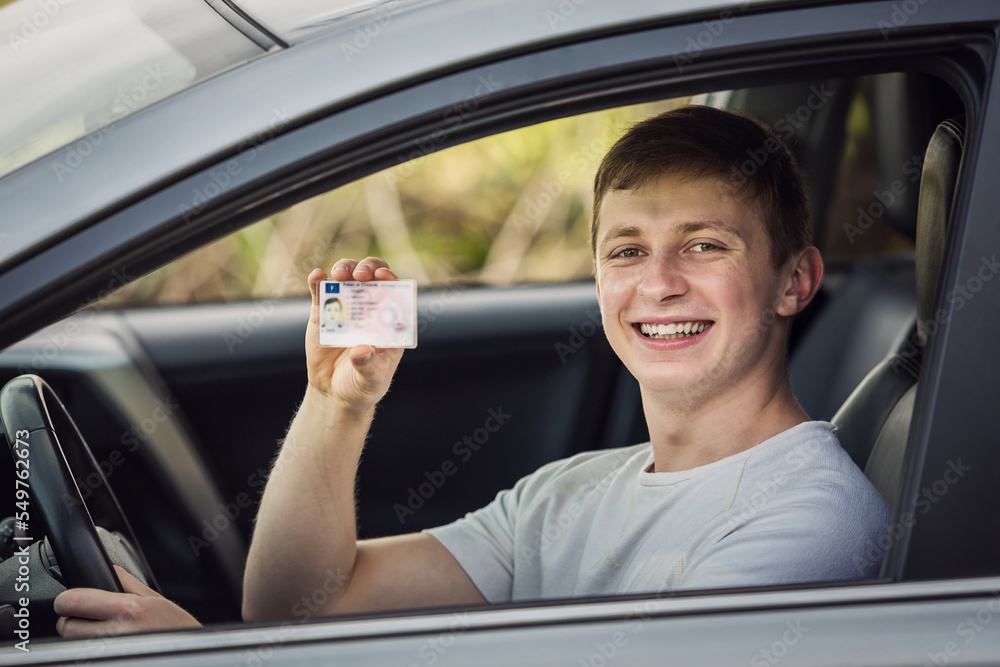 Happy and proud guy showing his driver license out of the car window ...