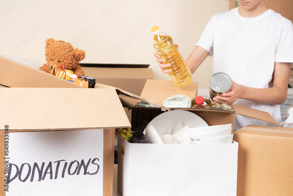 Teenage boy volunteer collecting food into donation box. Donation ...