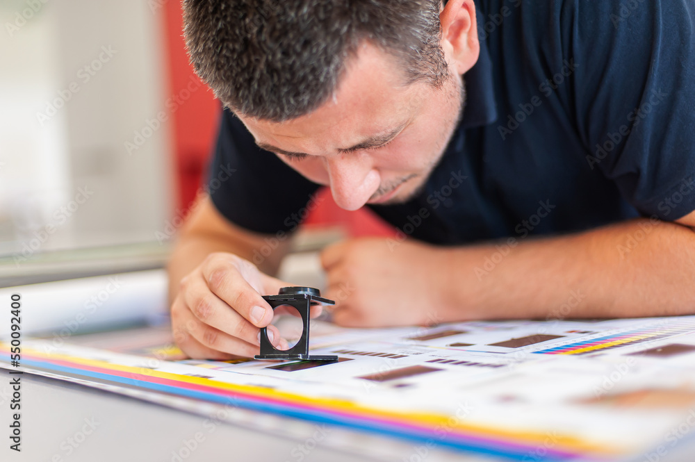 Young man in the process of printing used color scales and loupe and ...