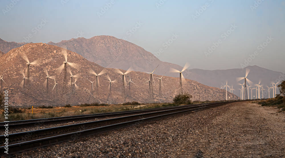 railroad tracks pass through a windmill farm as turbine tune to create ...