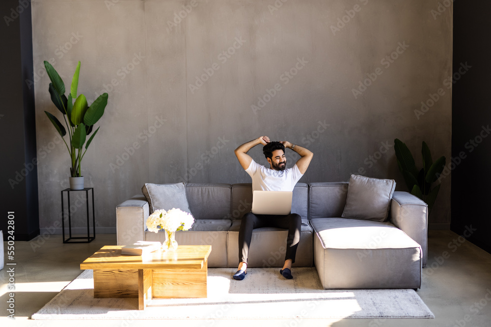 Great News Concept. Joyful guy using pc sitting on couch in living room ...