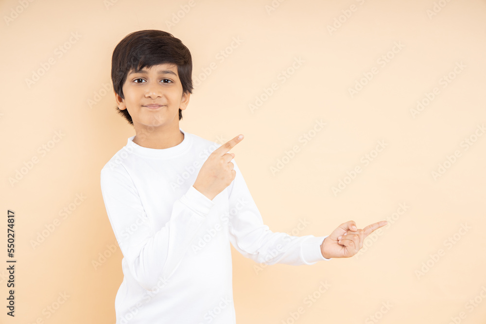 Happy Indian boy child wearing white t-shirt pointing finger at blank ...