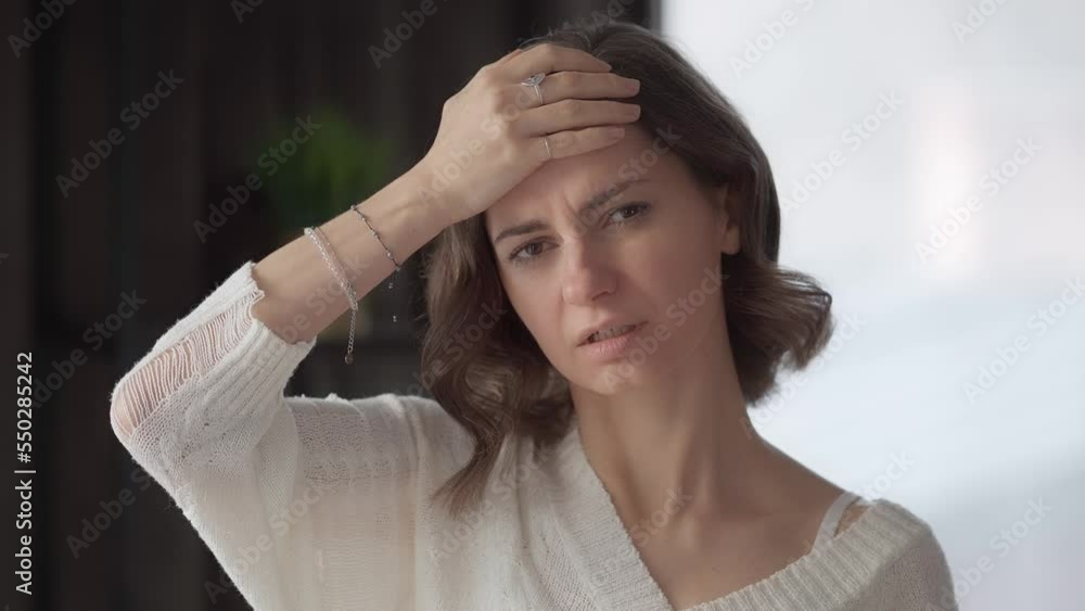A young woman at home touches her forehead with her hand to check her ...