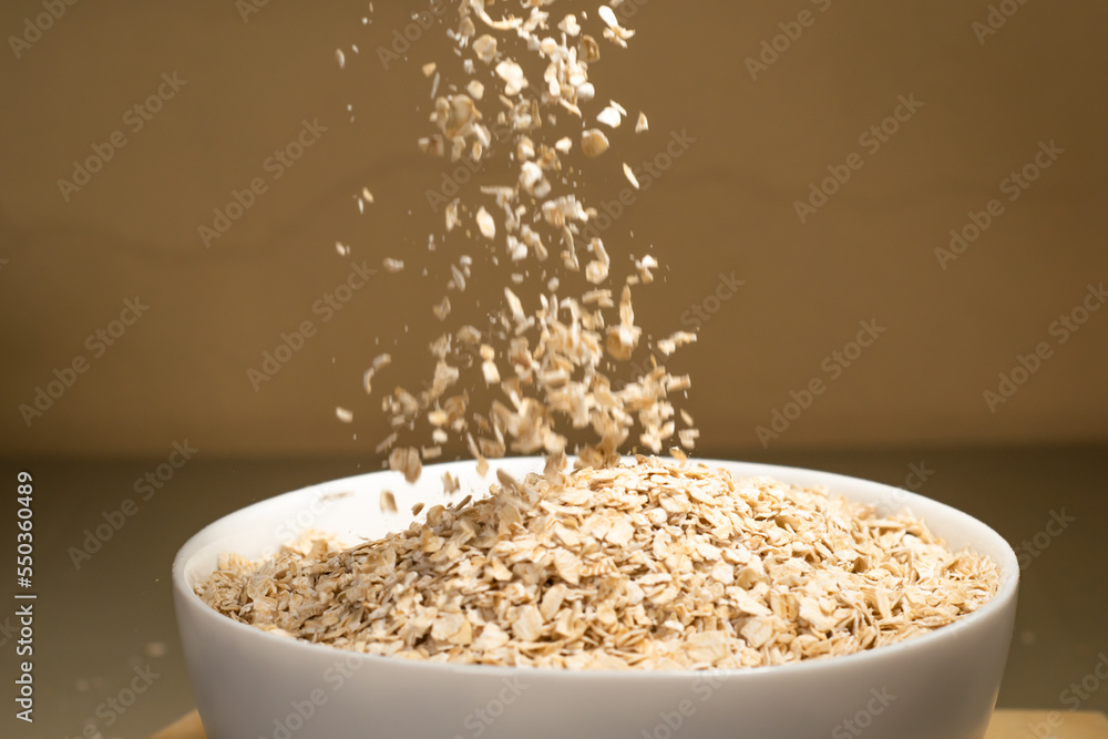 Avena molida siendo vertida en un bol blanco con una cuchara de metal ...