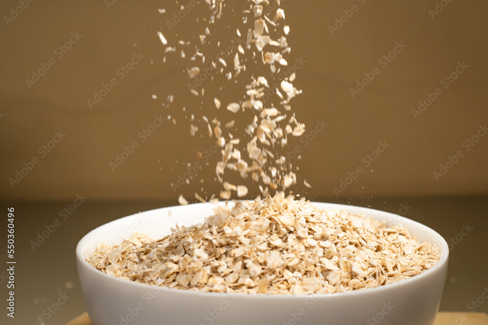 Avena molida siendo vertida en un bol blanco con una cuchara de metal ...