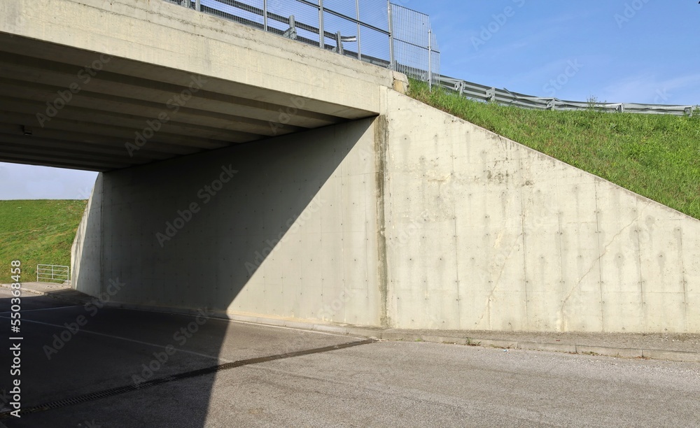 Side view of a concrete road bridge, with grass and guard rail in entry ...