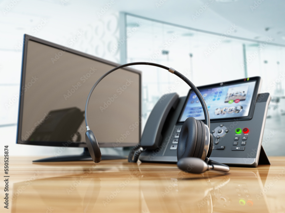 Modern VoIP phone and headset standing on wooden office table. Call ...