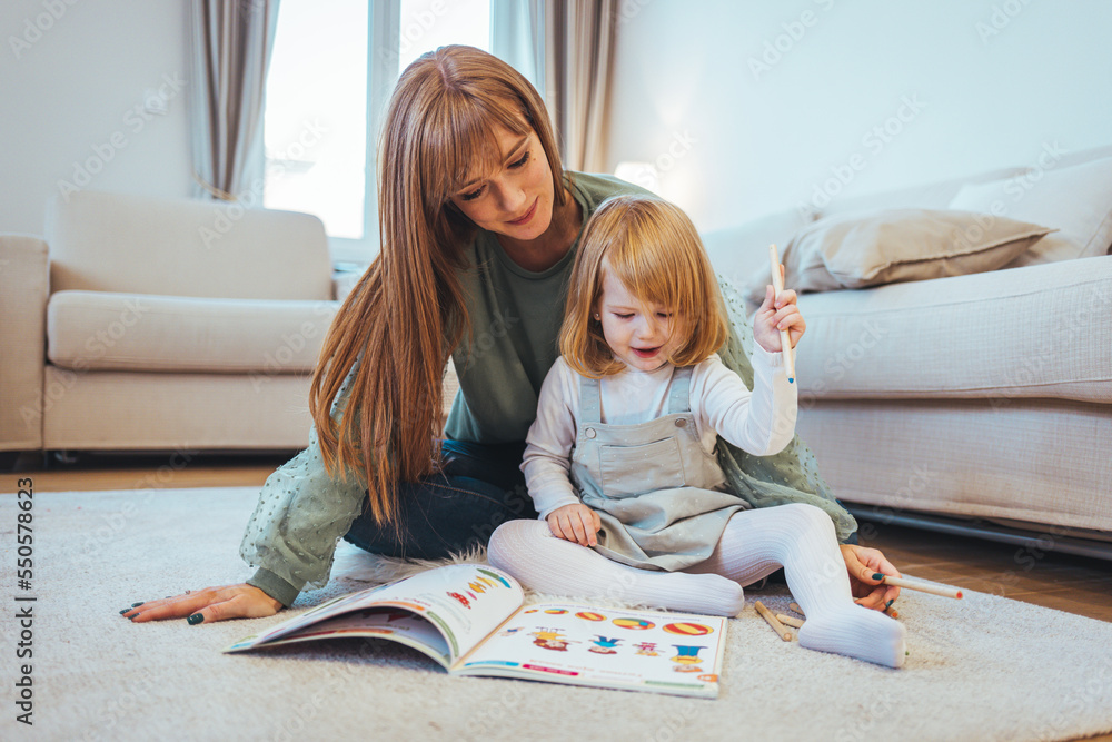 Caring smiling mother reading book with little kid girl lying on warm ...