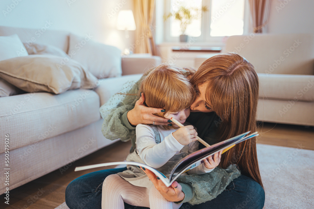 Caring smiling mother reading book with little kid girl lying on warm ...