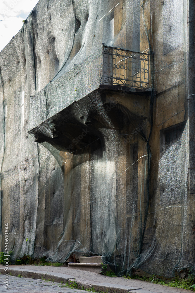 Old multi-storey building with balcony closed with construction grid ...