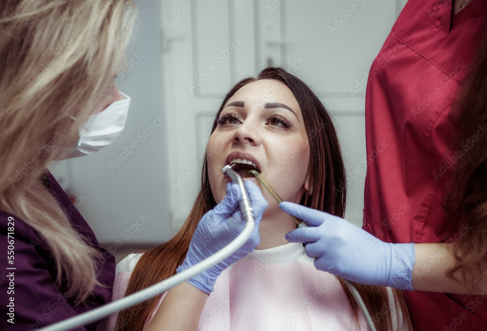Female dentist with an assistant uses a dental drill in a dental clinic ...