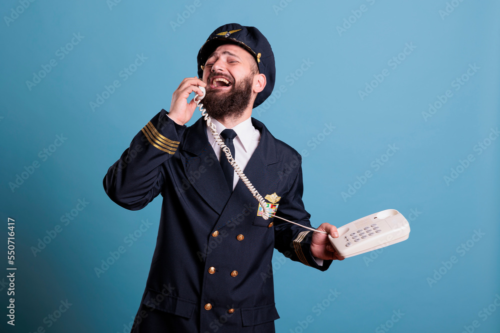 Middle aged airliner captain talking on landline phone, holding ...