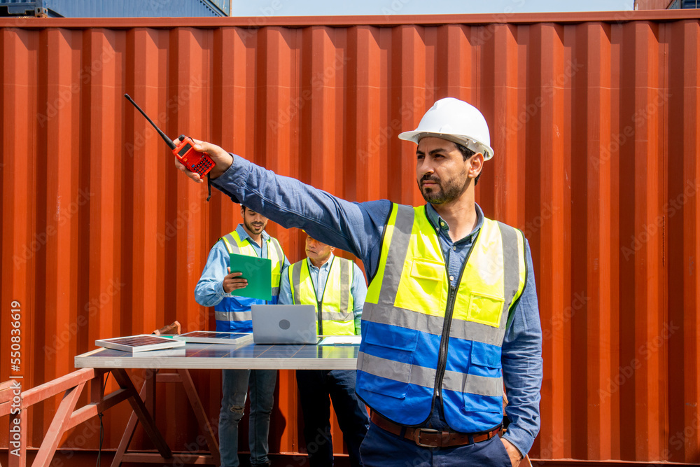 Supervisor in helmet and uniform using walkie-talkie in front of ...
