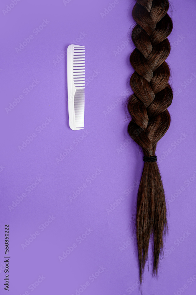 A braid of dark hair on a purple background with a comb. Braided hair ...