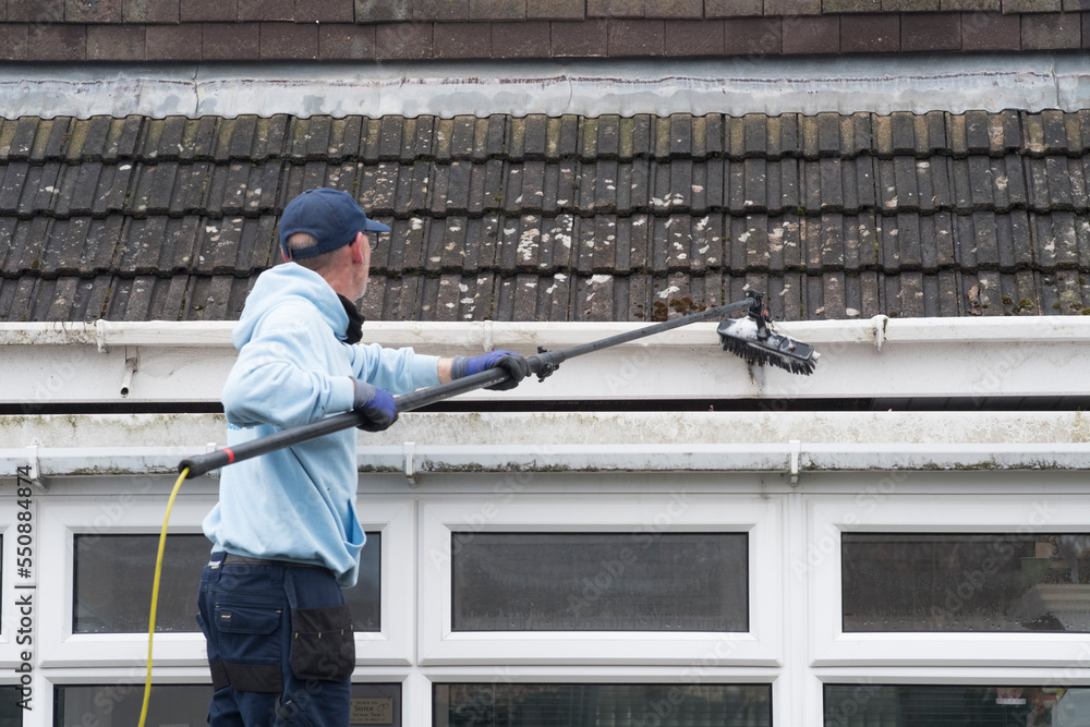 A window and gutter cleaner cleaning Dirty clogged white plastic pvc ...