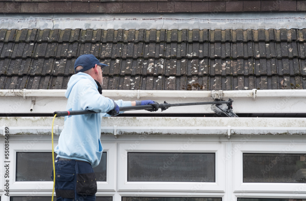 A window and gutter cleaner cleaning Dirty clogged white plastic pvc ...