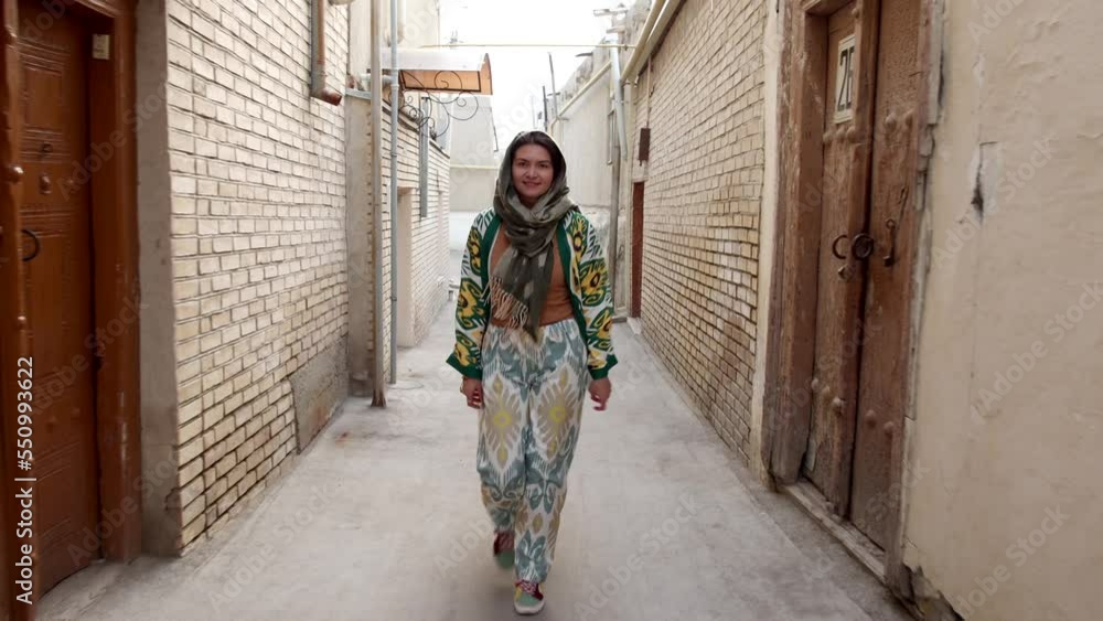 A girl in an Uzbek traditional robe walks through the old city of ...