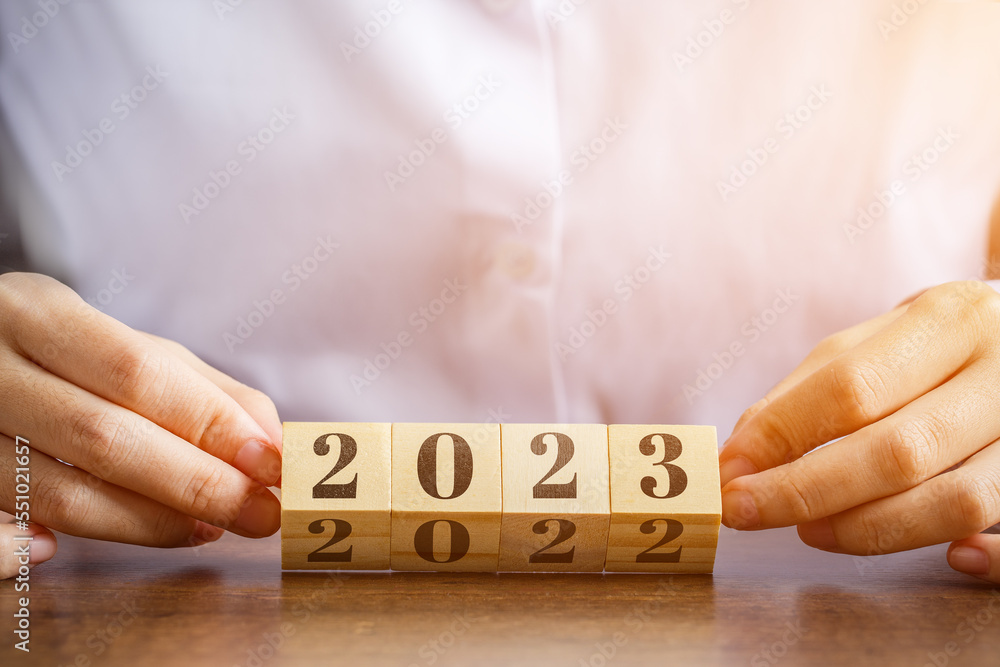 Foto de Hand holding wooden blocks with numbers indicating year 2022 flipped to 2023. Concept of ...