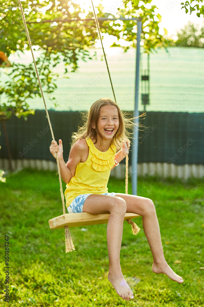 Happy barefoot laughing child girl swinging on a swing in sunset summer ...