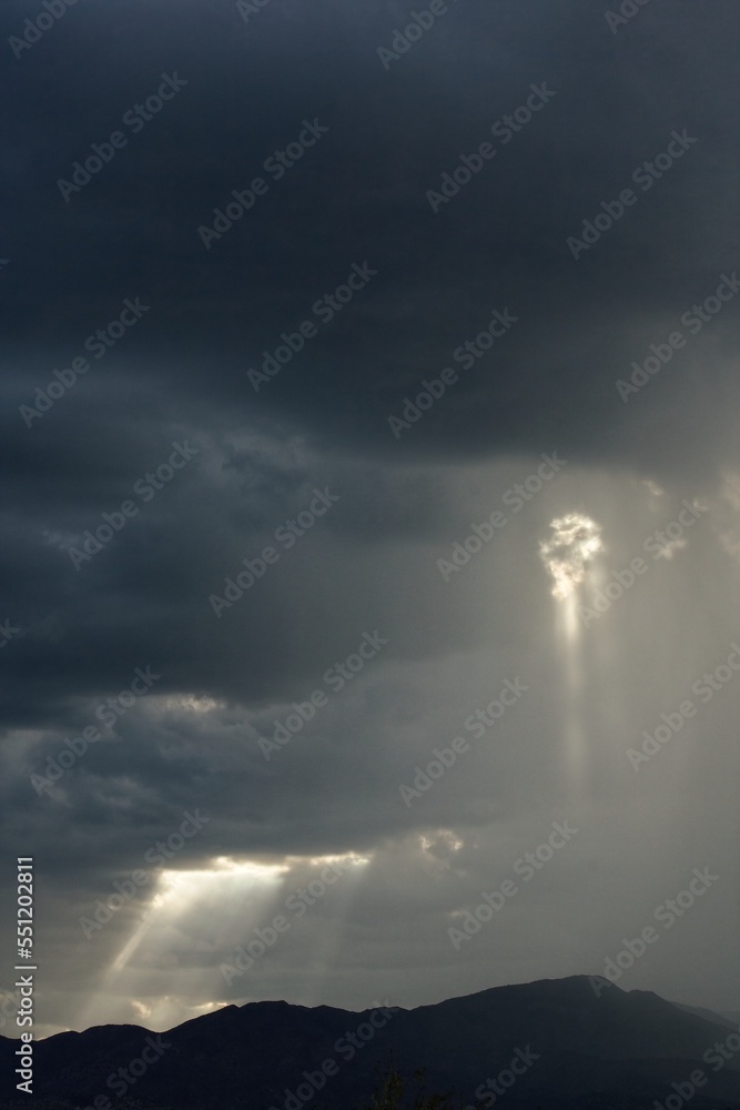 Sunbeams pierce a rain cloud with rain to one side and mountains below ...