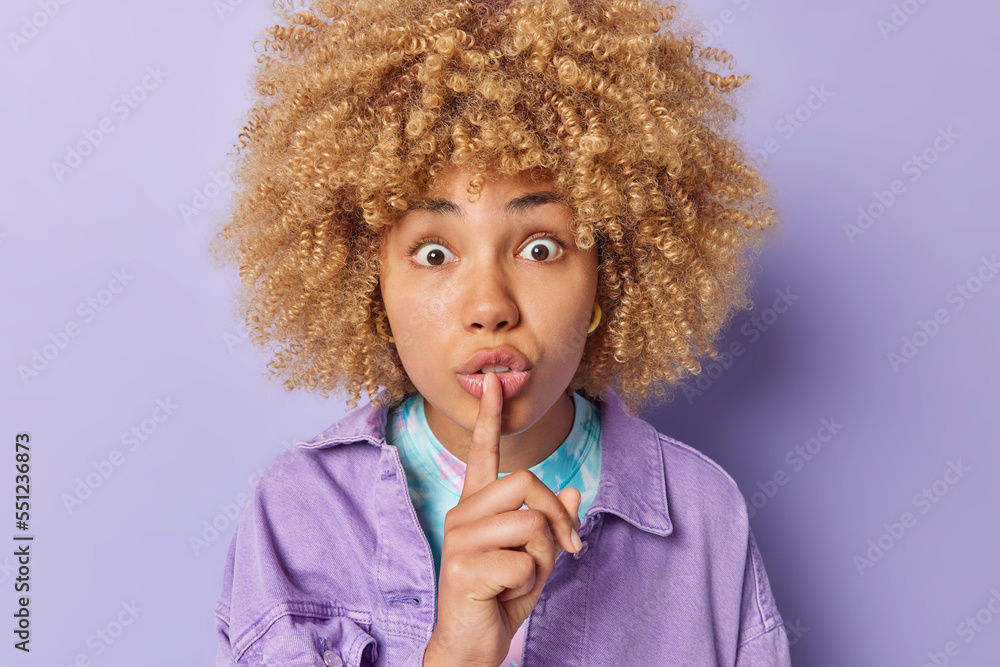 Photo of surprised curly haired woman make silence gesture keeps index ...