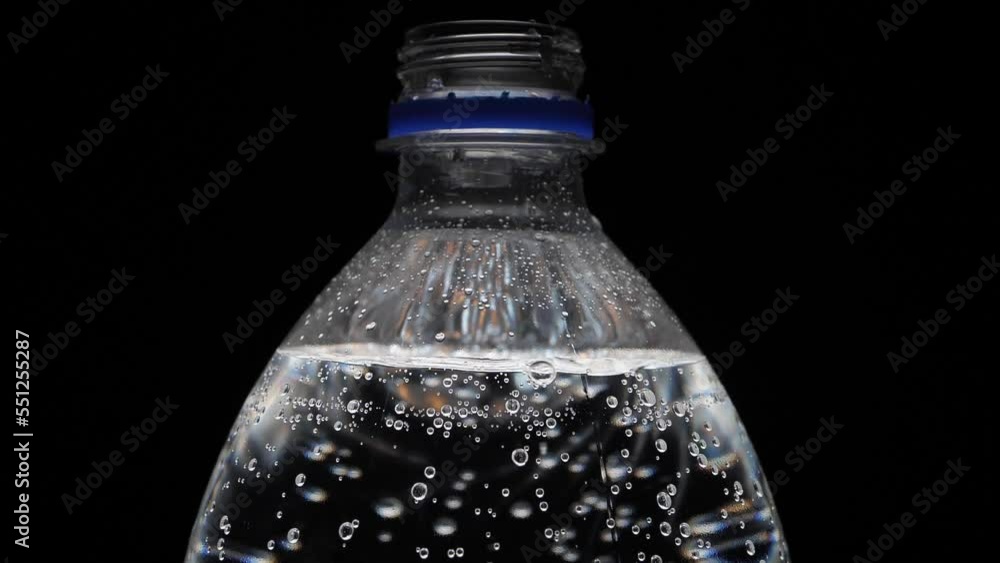 A bottle of carbonated water is unscrewed by hand on a black background ...