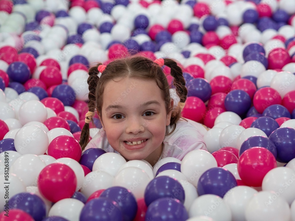 A happy little girl with two pigtails in a large dry children's pool ...