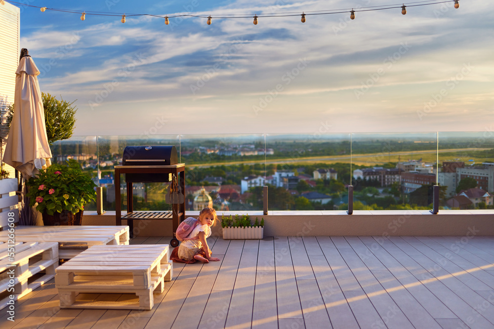 cute baby girl sitting on sunlit rooftop patio at summer evening with ...