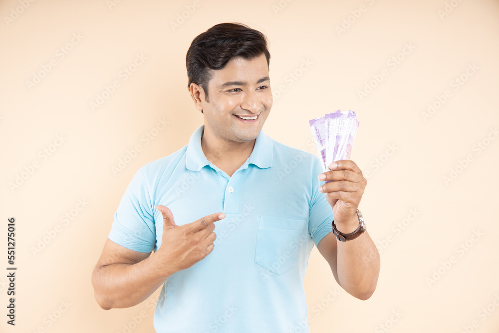 Portrait of happy Indian man pointing at rupee notes isolated on beige ...
