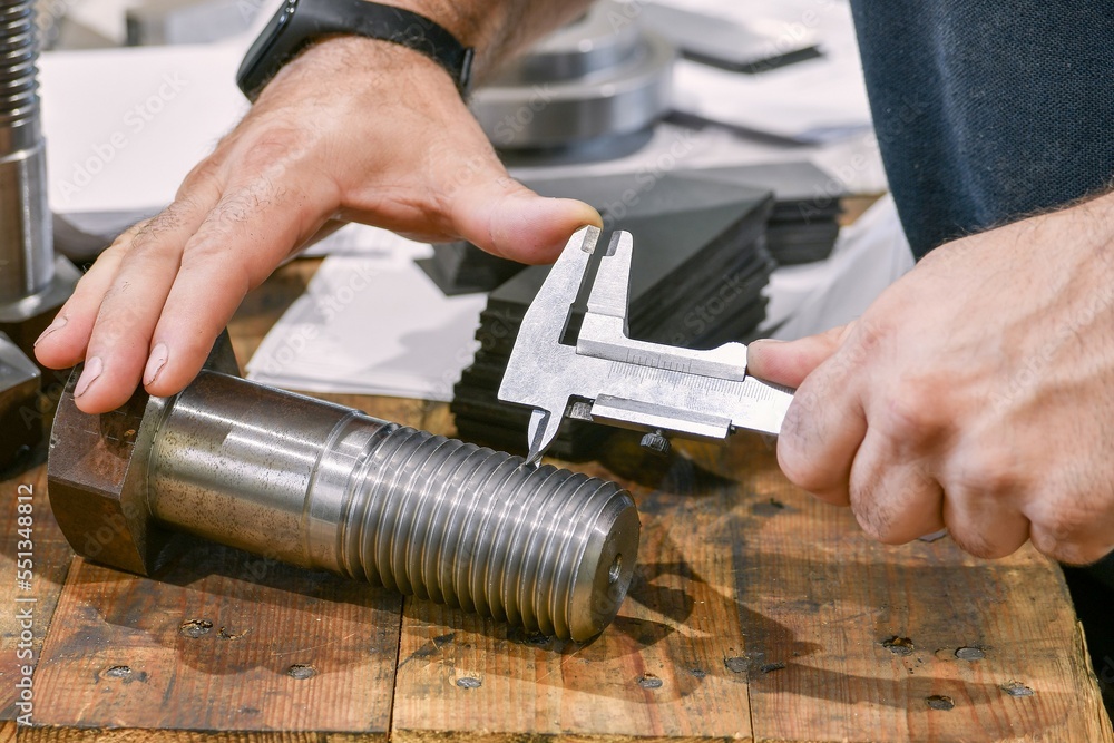 The worker measures the thread pitch on the bolt with a vernier caliper ...